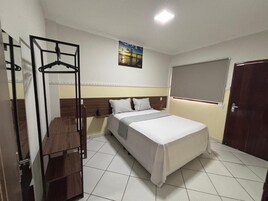 Quarto com cama, mesa de madeira, cabideiro e janela.