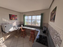 Cozinha equipada com geladeira, pia, dois banquinhos, janela com vista e liquidificador.
