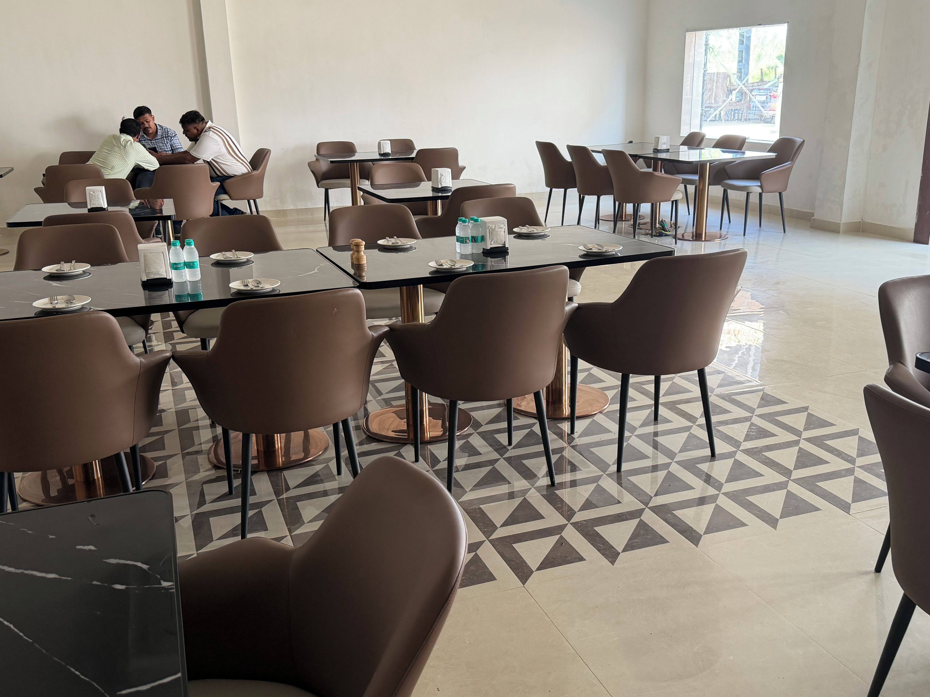 Sala de conferências com várias mesas e cadeiras, equipada com garrafas de água e guardanapos.