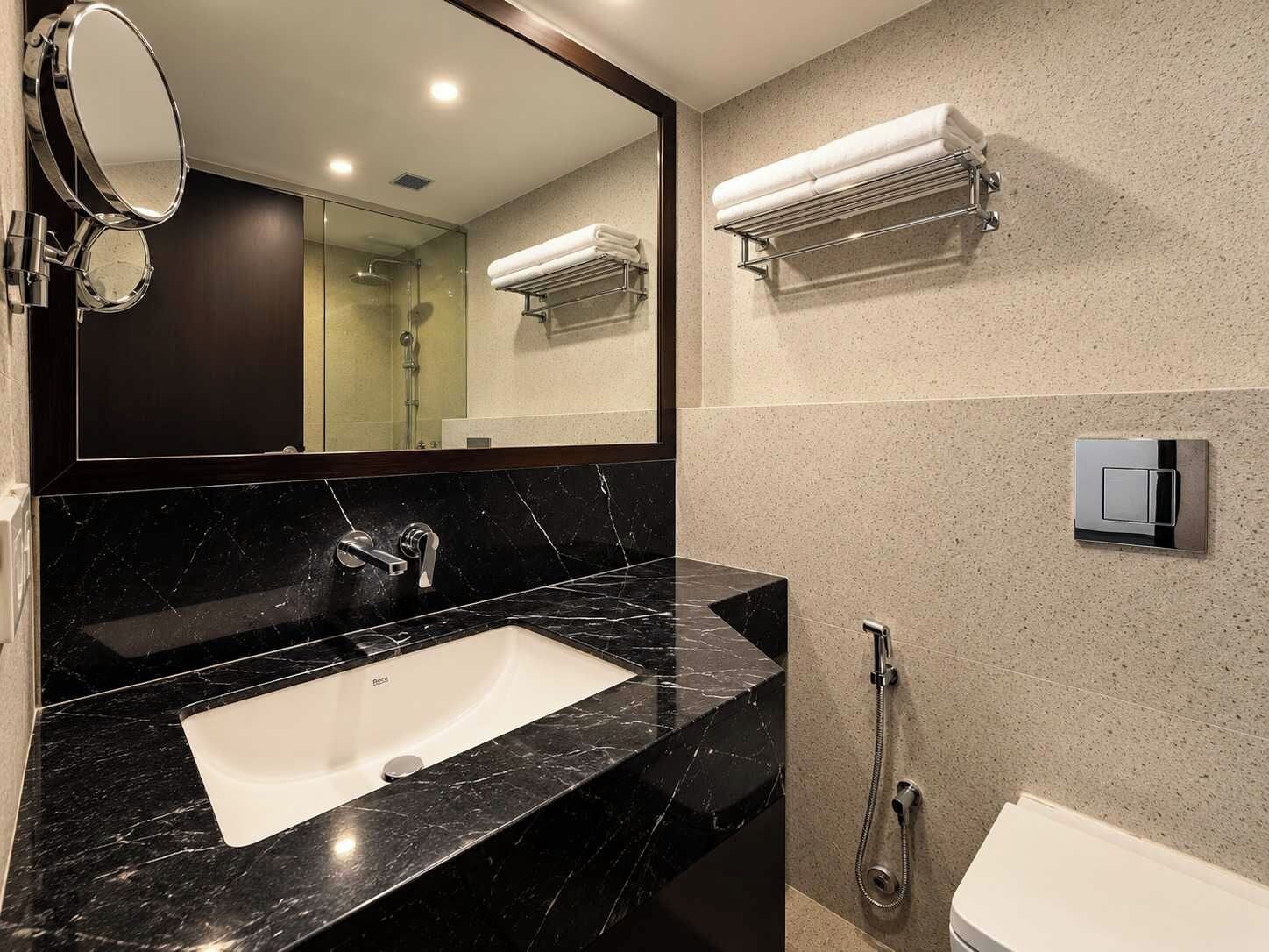 Um banheiro moderno com uma pia de mármore preto, um espelho grande, porta-toalhas e chuveiro.