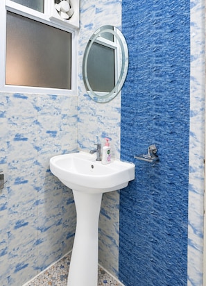Casa de banho com lavatório pedestal branco, espelho redondo e parede azul com textura.