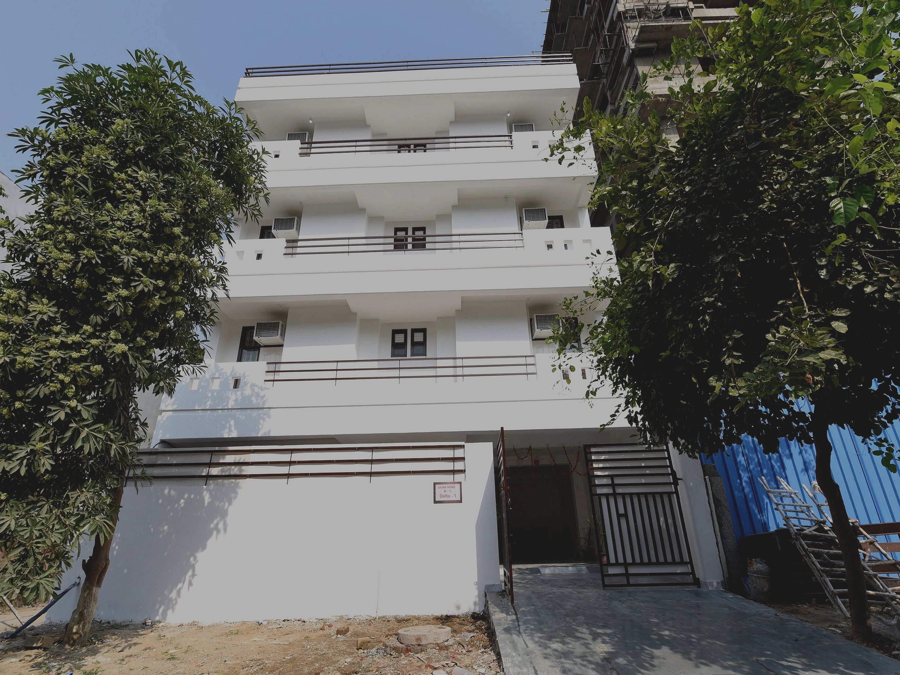 Um edifício residencial com vários andares, varandas, entrada com portão e uma cerca azul ao fundo.