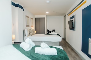 Quarto de hotel com cama, escrivaninha, cadeira e televisão.
