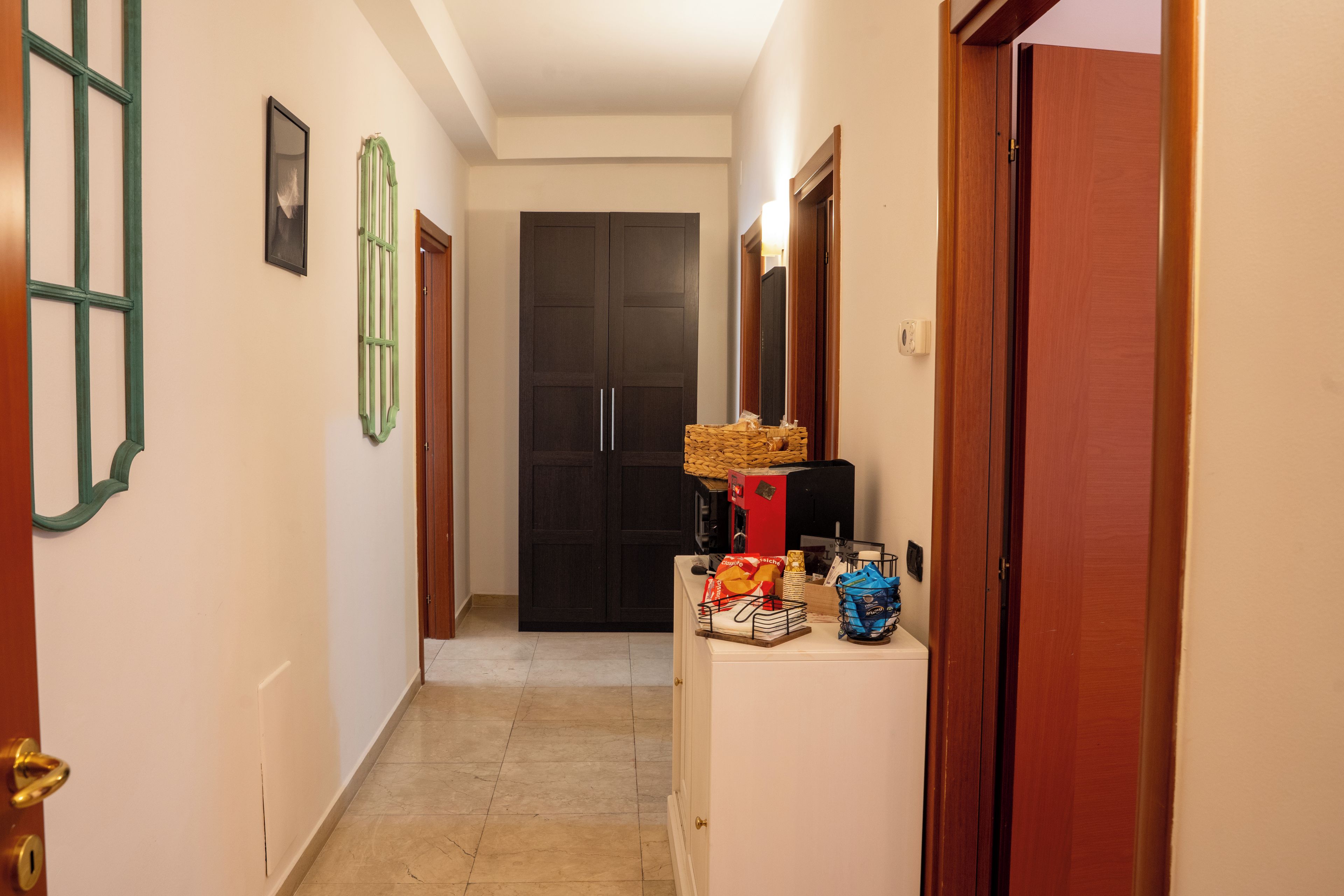 Corredor com chão ladrilhado, porta preta no final e um balcão com lanches e uma cesta.