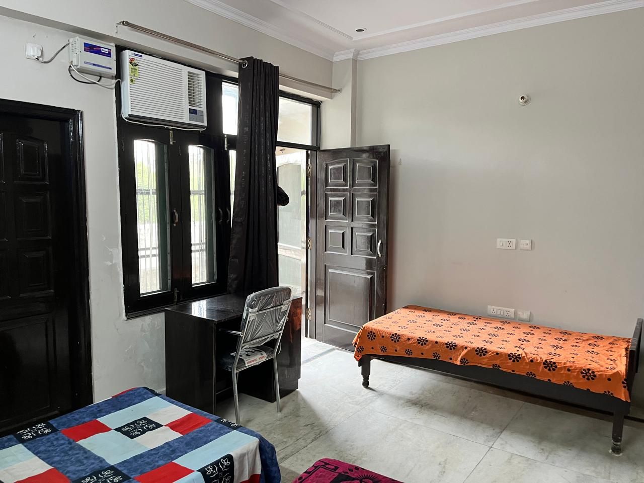 Quarto com cama, escrivaninha, cadeira e aparelho de ar condicionado.