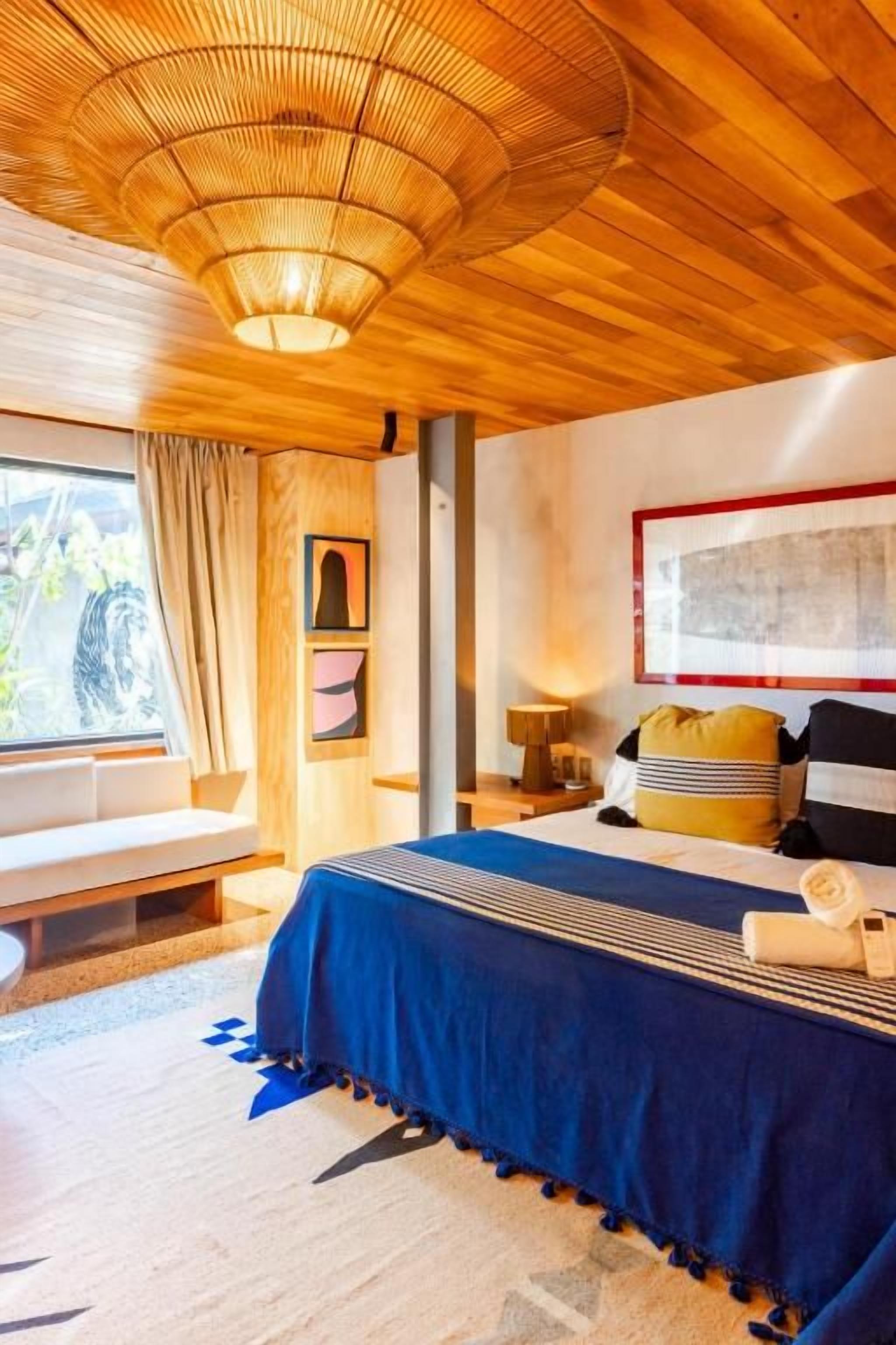 Quarto com cama, janela com cortinas, obra de arte na parede e teto de madeira.