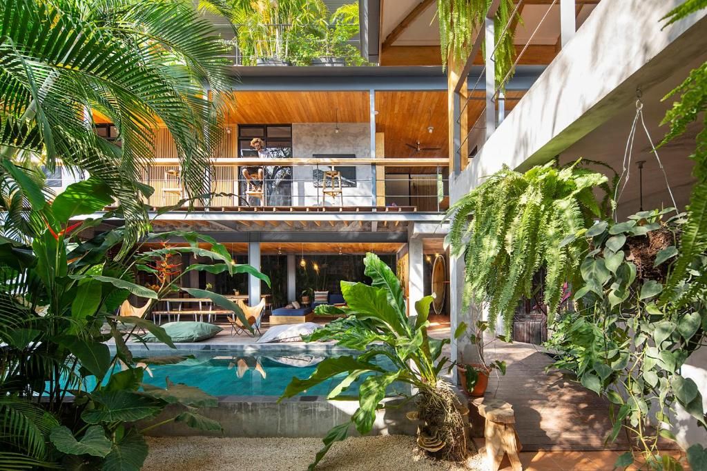 Um edifício residencial moderno, com vários andares, piscina, área de estar externa e vegetação exuberante.