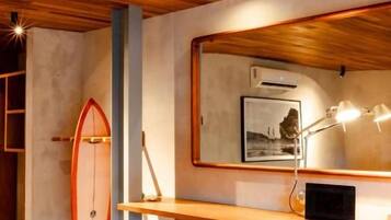 Quarto com escrivaninha de madeira, cadeira, prancha de surf e uma moldura na parede.