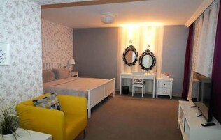 Um quarto com uma cama, uma escrivaninha, duas cadeiras, um espelho e uma televisão.