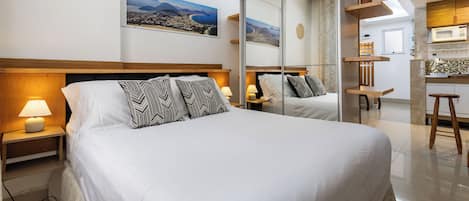 Quarto de hotel moderno com cama grande, mesa de cabeceira, luminária, espelho e vista para a cidade.