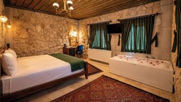 Quarto com cama, escrivaninha, cadeira, banheira com pétalas de rosa e parede de pedra.