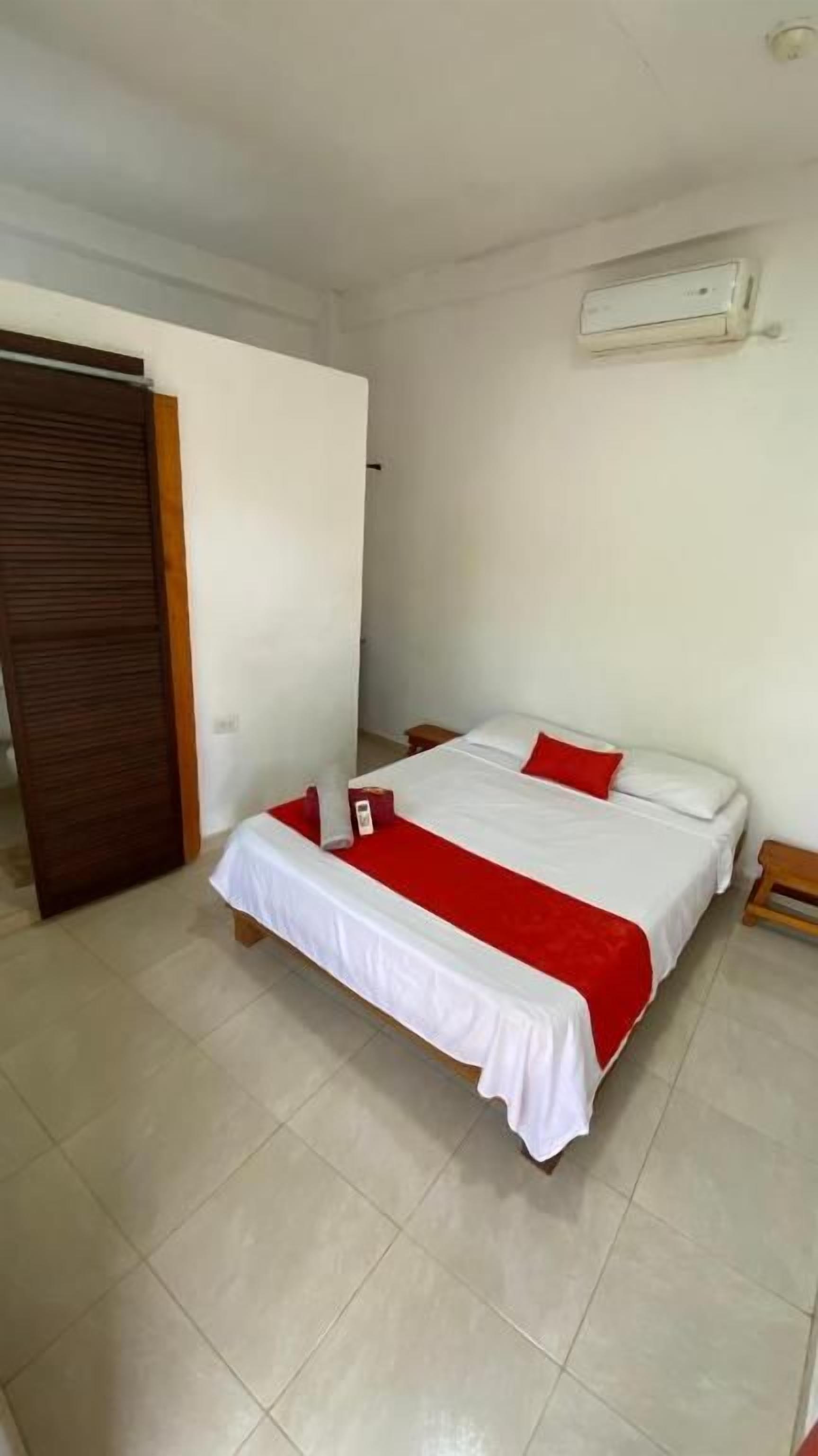 Quarto com cama, mesa de cabeceira, guarda-roupa e ar condicionado.