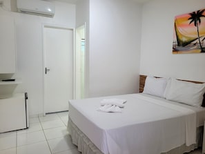 Quarto de hotel com cama, parede branca, quadro e porta.