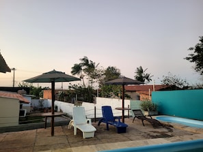 Área da piscina com espreguiçadeiras, guarda-sóis e uma pequena mesa.