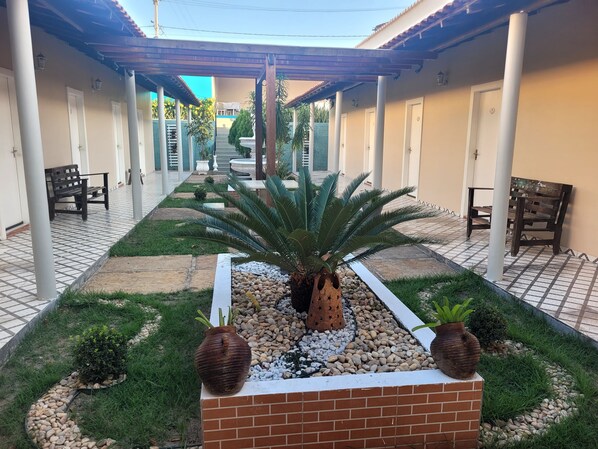 Área externa coberta com bancos, uma planta central e um caminho que leva a um edifício.