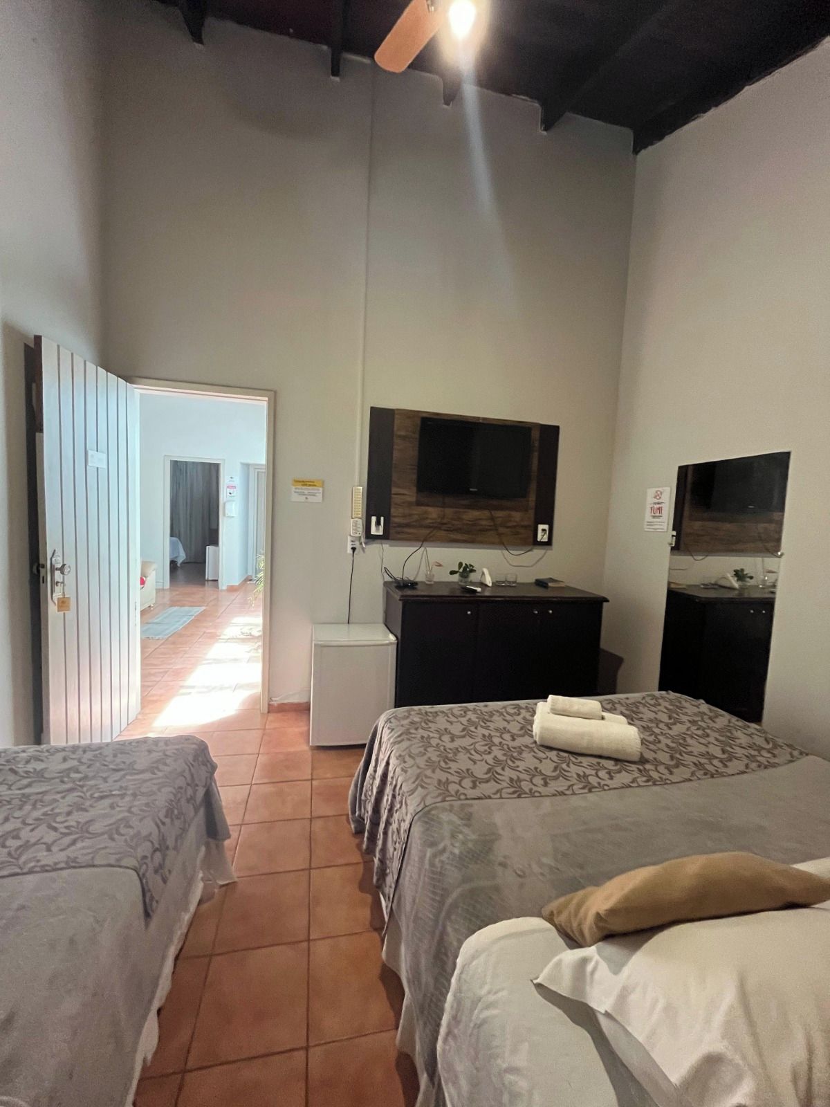 Quarto de hotel com duas camas, uma escrivaninha, uma televisão e uma porta que dá para outro espaço.