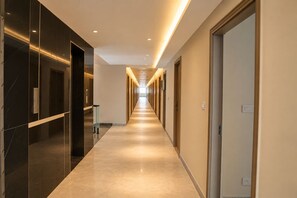 Corredor longo e bem iluminado, com portas de ambos os lados, que dá acesso a quartos individuais.