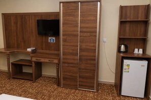 Quarto compacto com escrivaninha, televisão, frigorífico e armário.