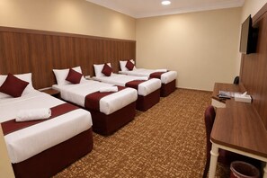 Quarto de hotel com quatro camas, uma escrivaninha e uma televisão.
