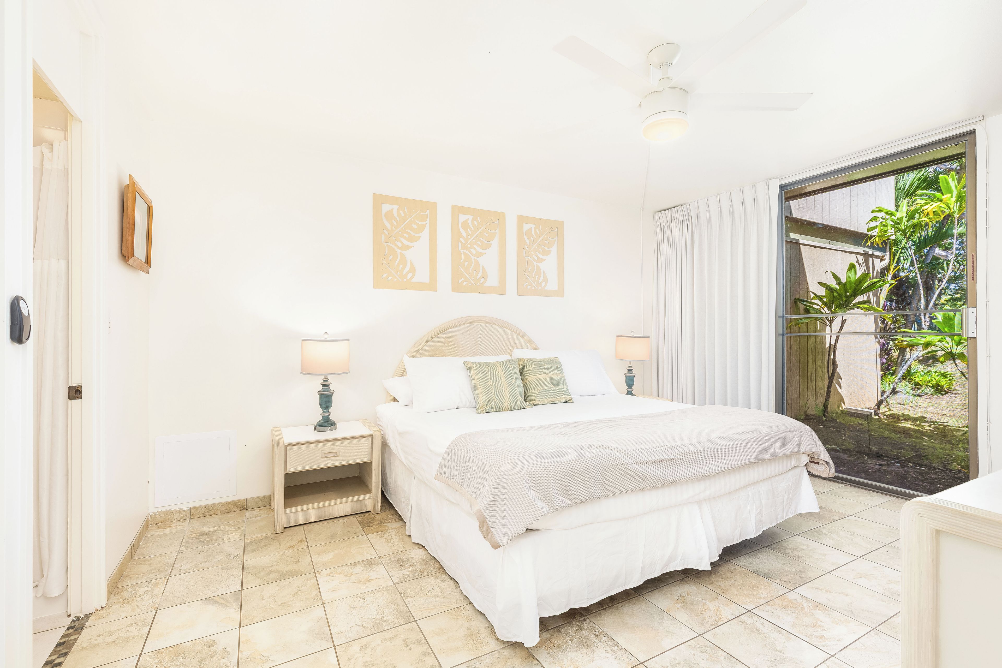 Quarto com cama, duas mesas de cabeceira, ventoinha no teto e vista para o exterior.