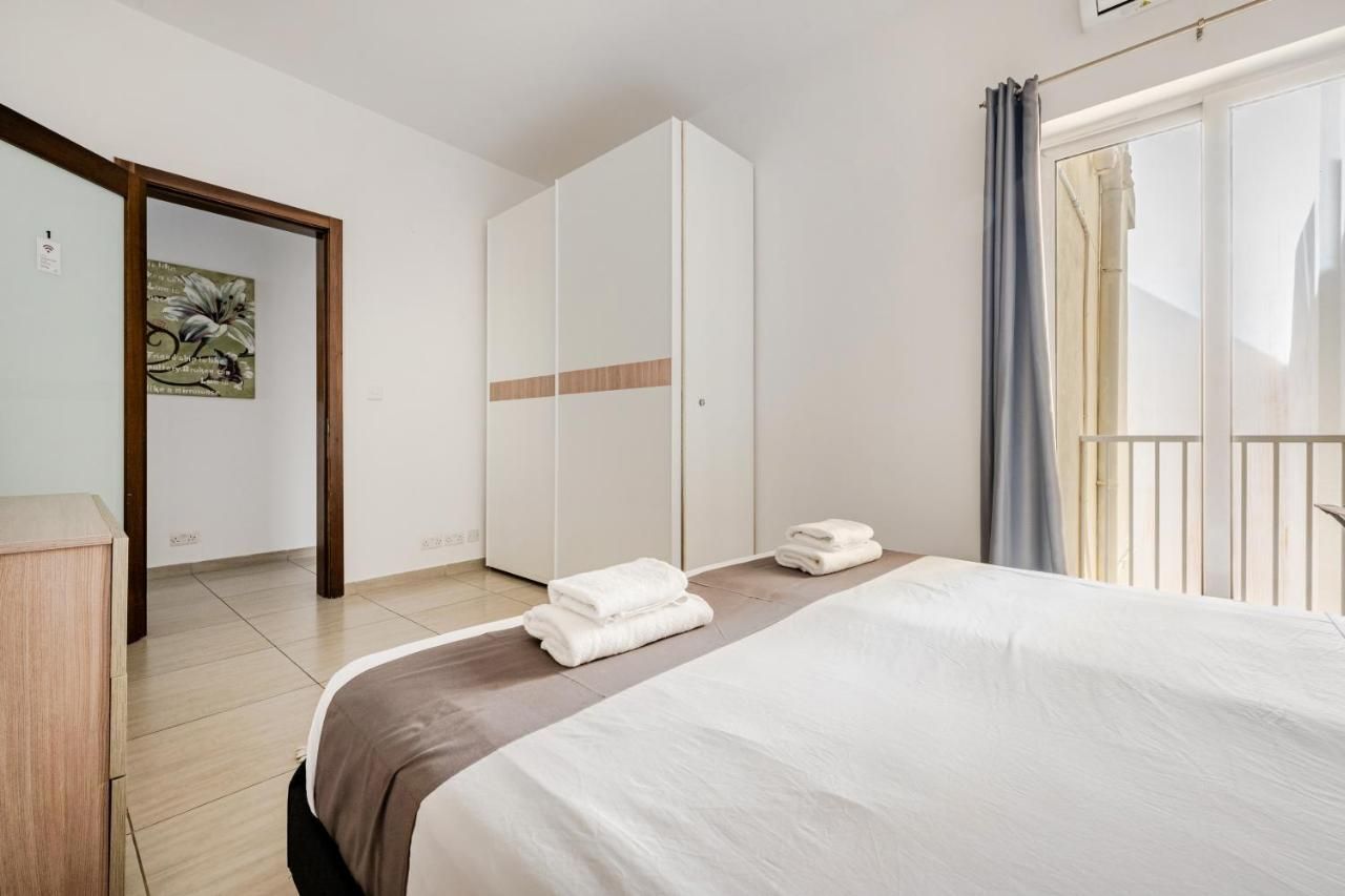 Quarto de hotel com cama, guarda-roupa, porta que dá para outro aposento e janela com cortinas.