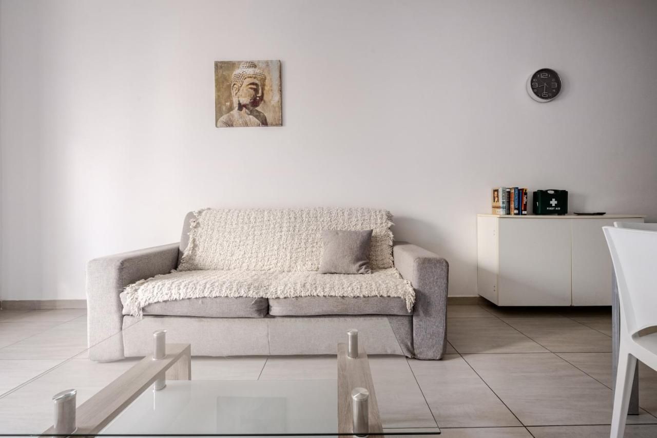 Sala de estar minimalista com sofá, mesa de centro de vidro, relógio fixado na parede e estante de livros.