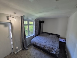 Quarto com cama, janela, porta e luminária no teto.