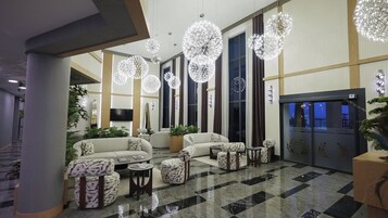 Um saguão de hotel com piso xadrez, área de estar com sofás estampados e luminárias esféricas decorativas.
