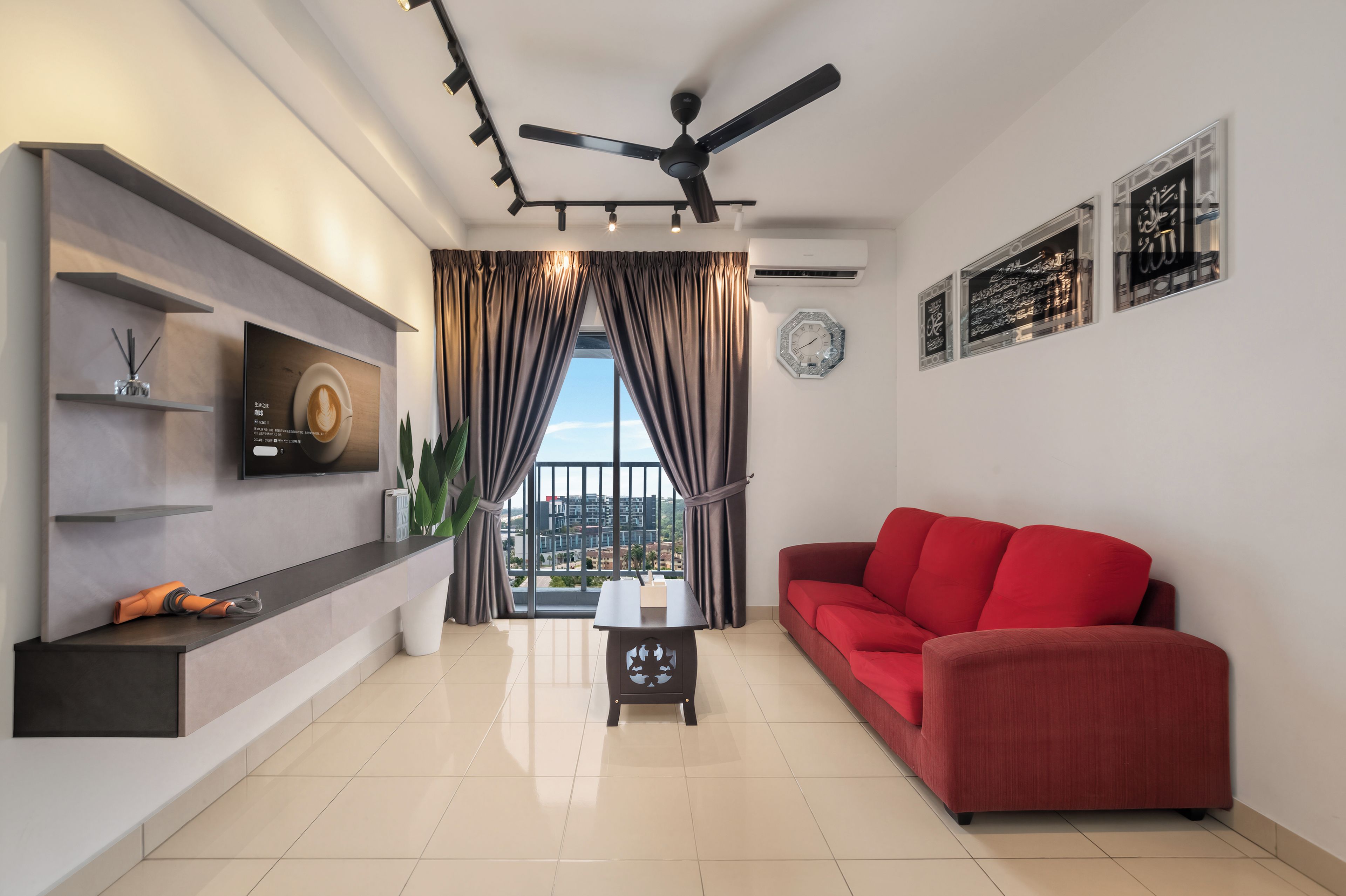 Uma sala de estar moderna com um sofá vermelho, televisão de tela plana, ventilador de teto e vista para edifícios através de grandes janelas.