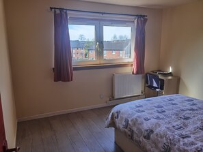 Quarto com cama, radiador, televisão e janela com cortinas.