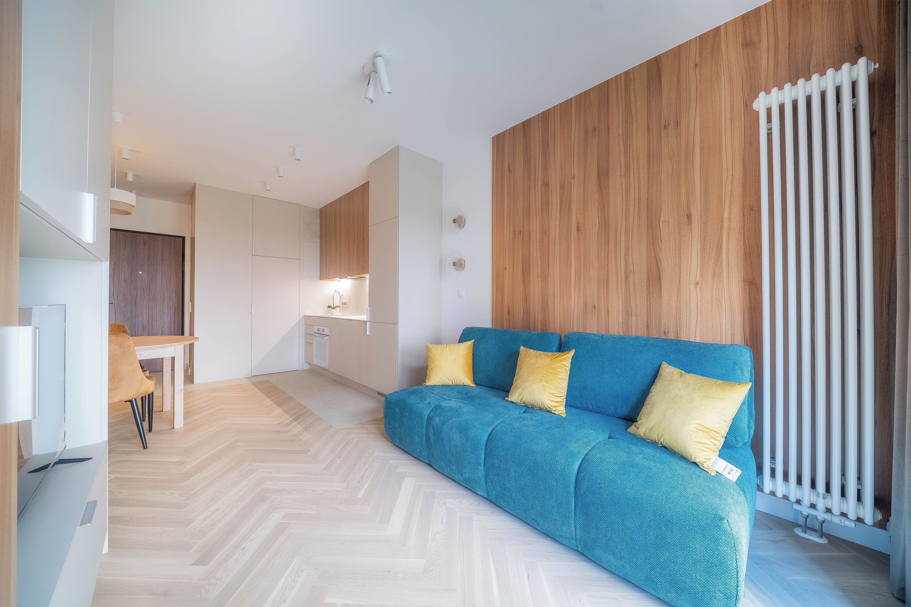 Uma sala de estar moderna com um sofá azul, lambris de madeira e um padrão de piso em herringbone.