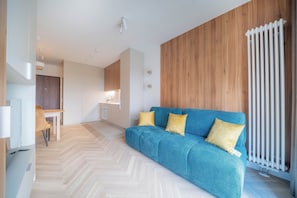Uma sala de estar moderna com um sofá azul, lambris de madeira e um padrão de piso em herringbone.