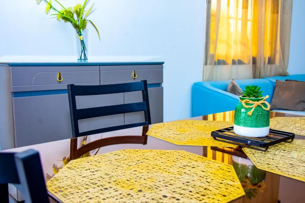 Uma sala de jantar com mesa e cadeiras, um vaso com flores e um sofá com almofada.
