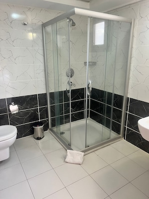 Um banheiro com chuveiro em gabinete de vidro, paredes com azulejos brancos e pretos, vaso sanitário branco e pia branca.