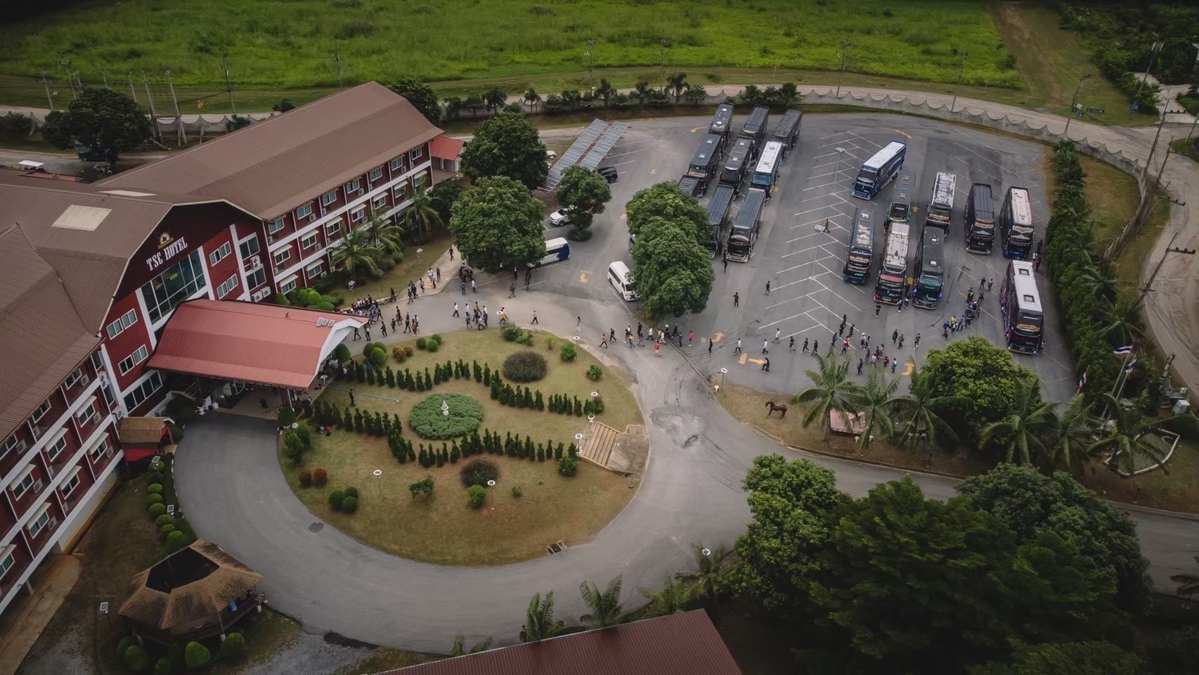 Um Hotel TSC com um pátio circular, um estacionamento com ônibus e um edifício com telhado vermelho.