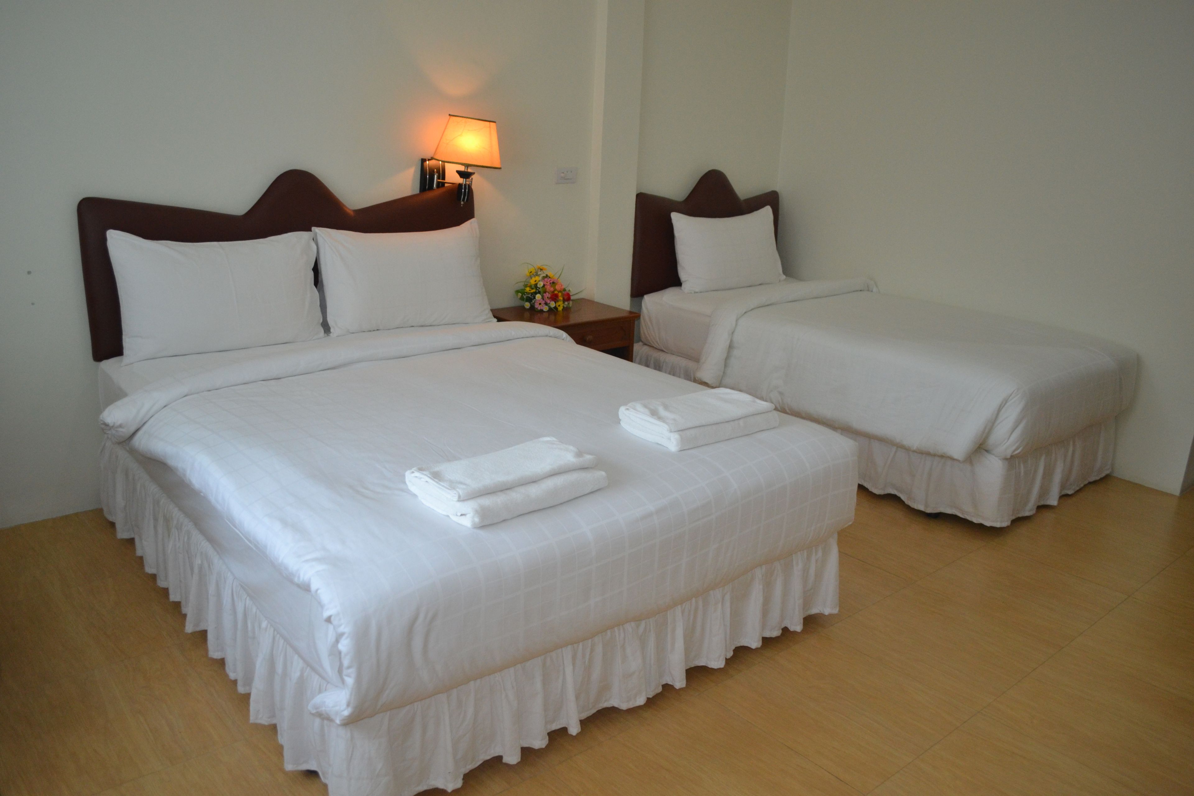 Uma cama de casal com cabeceira de madeira, roupa de cama branca e mesa de cabeceira com abajur e flores.