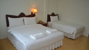 Uma cama de casal com cabeceira de madeira, roupa de cama branca e mesa de cabeceira com abajur e flores.