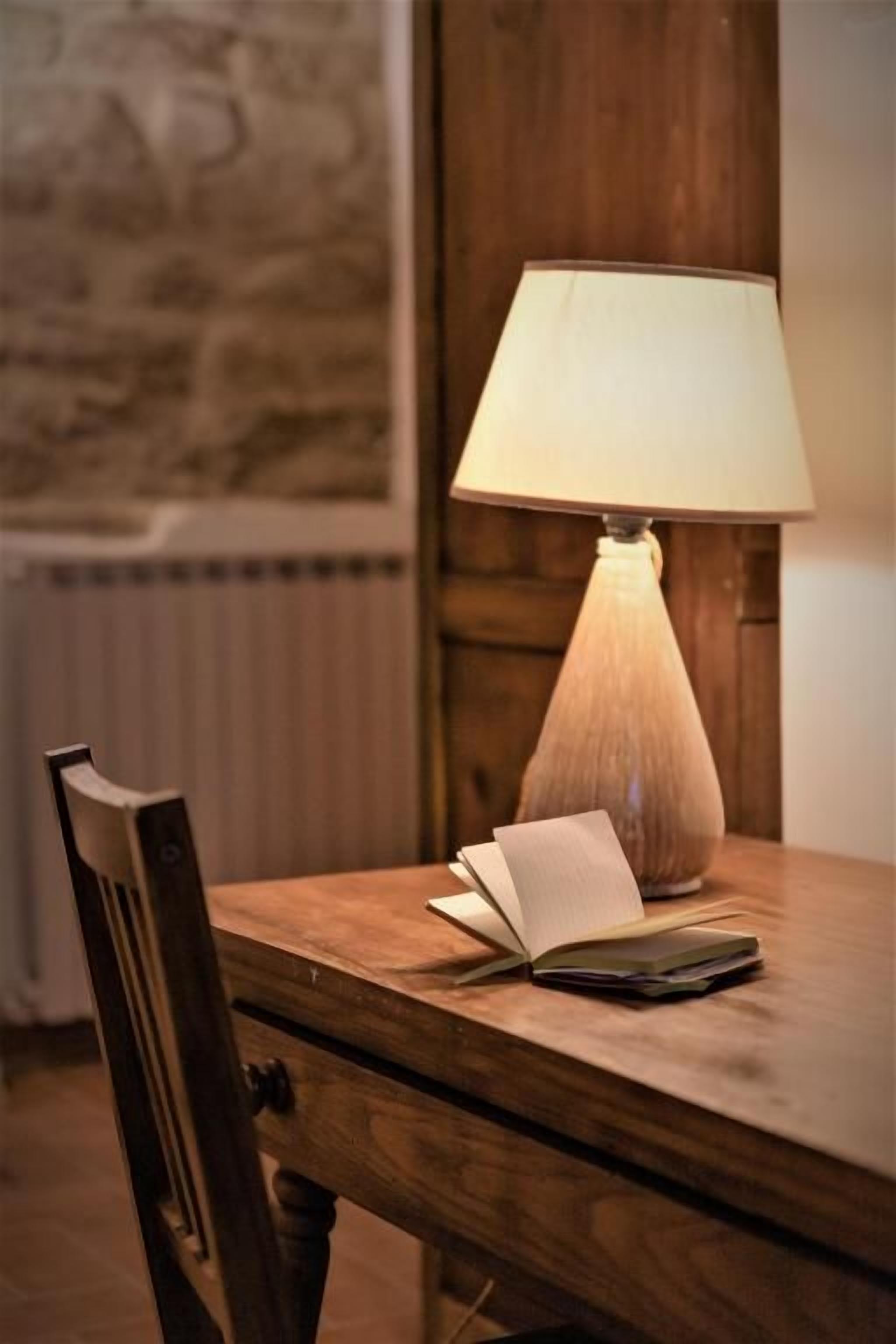 Uma mesa de madeira com uma lâmpada, um livro e uma carteira.