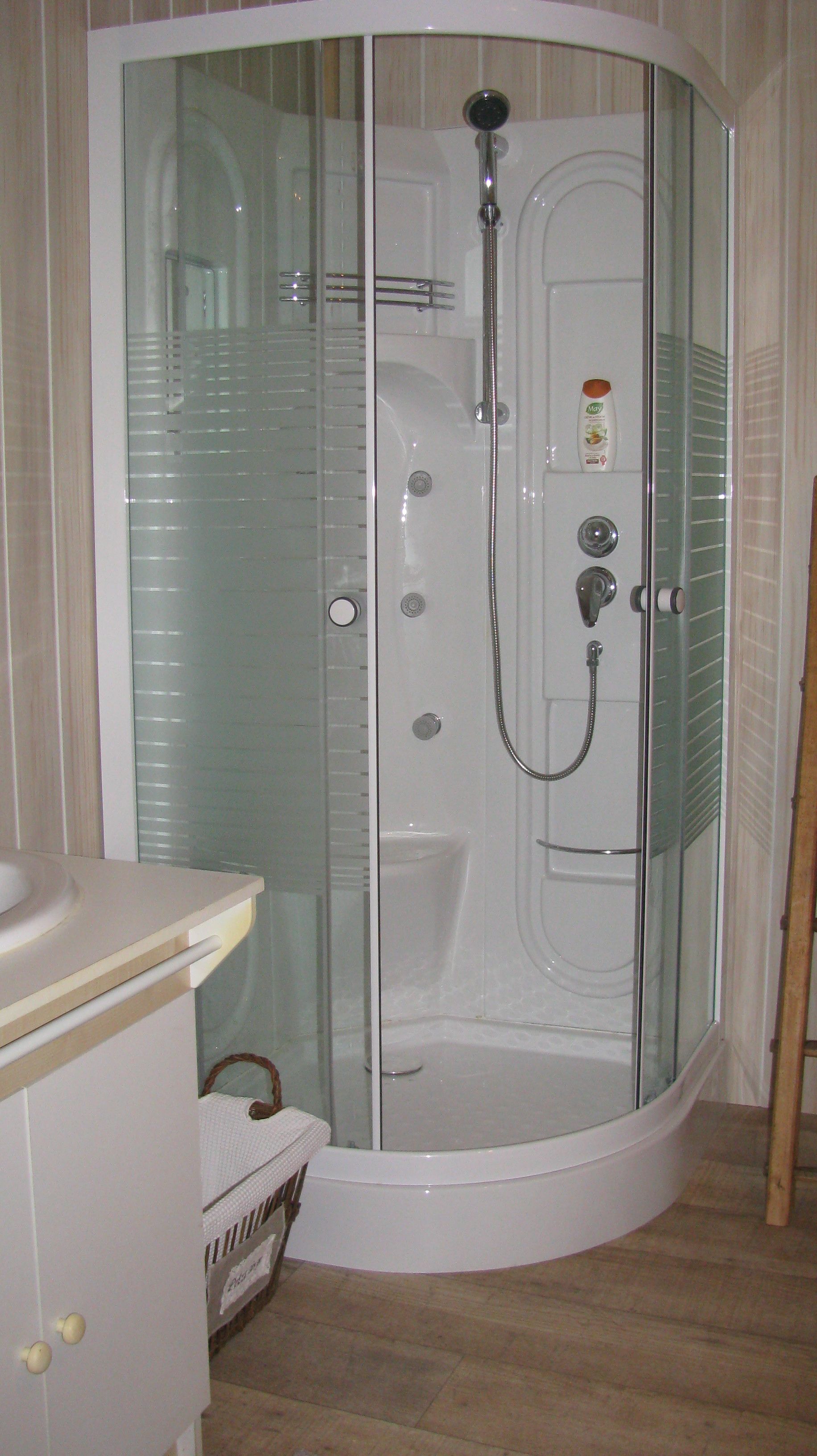 Box de chuveiro com paredes de vidro, chuveiro manual, painel de controle e uma garrafa de shampoo.