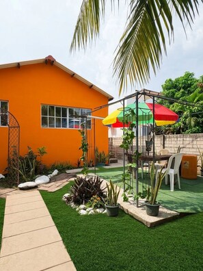 Um imóvel residencial com gramado bem cuidado, área de varanda com móveis de exterior e um guarda-sol colorido.
