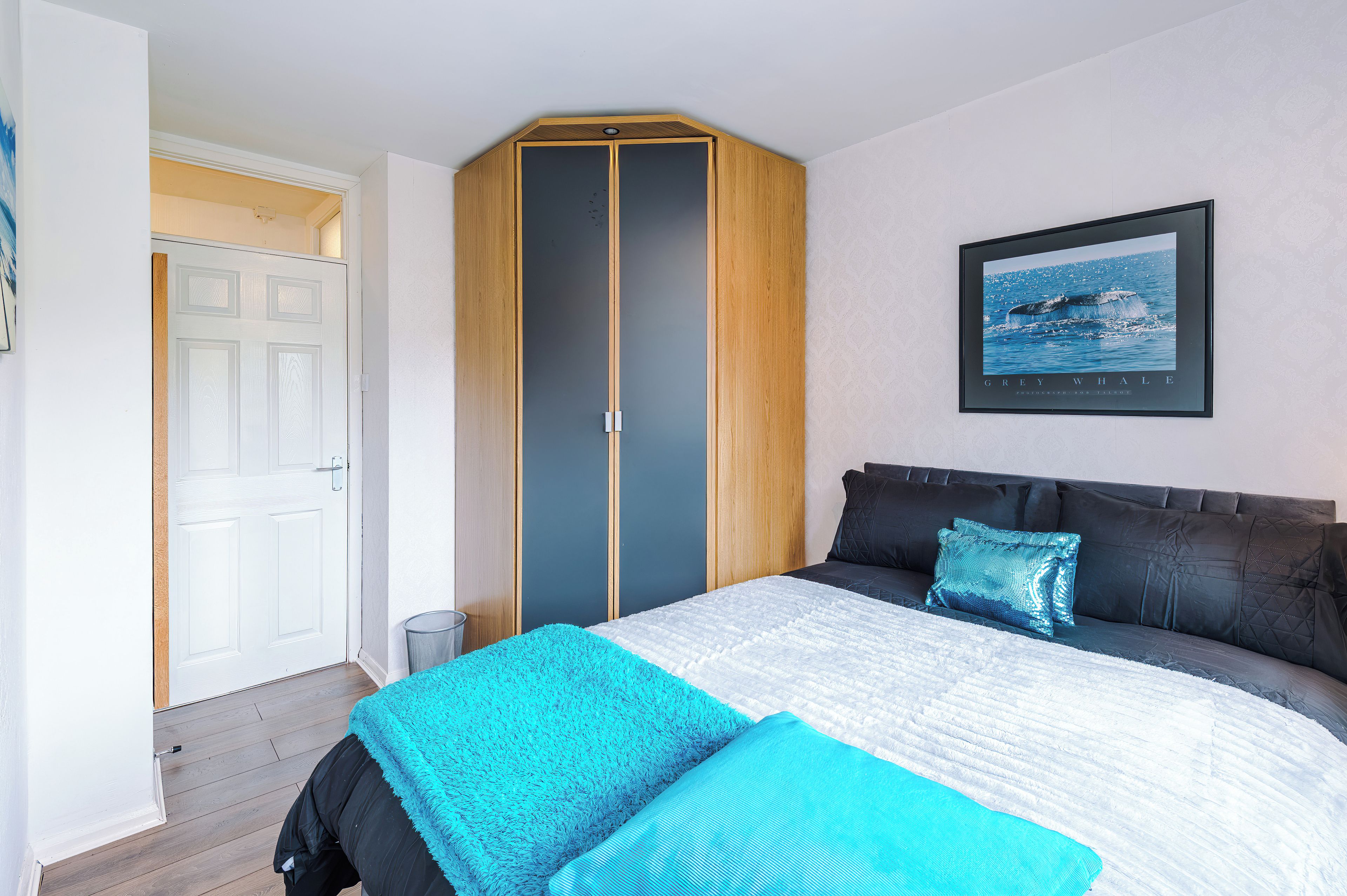 Quarto com cama, guarda-roupa, quadro na parede e porta para outro espaço.