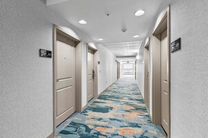 Corredor de hotel com portas numeradas 221 e 220, carpete estampado e teto com iluminação embutida.