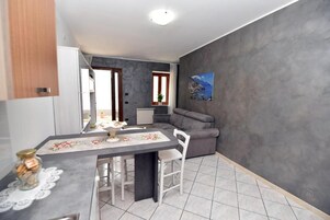 Espaço compacto com área de refeições, sofá cinza e vista para o exterior.