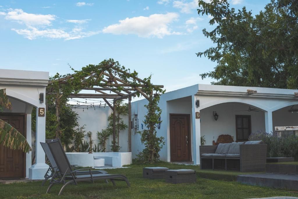 Área de pátio com pérgola, mobiliário externo e um edifício com fachada branca e portas em arco.