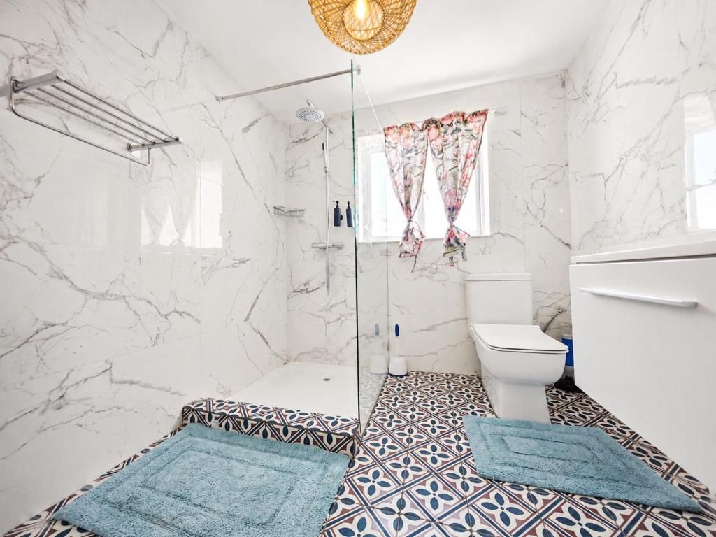 Casa de banho com chuveiro, sanita e ladrilhos estampados.