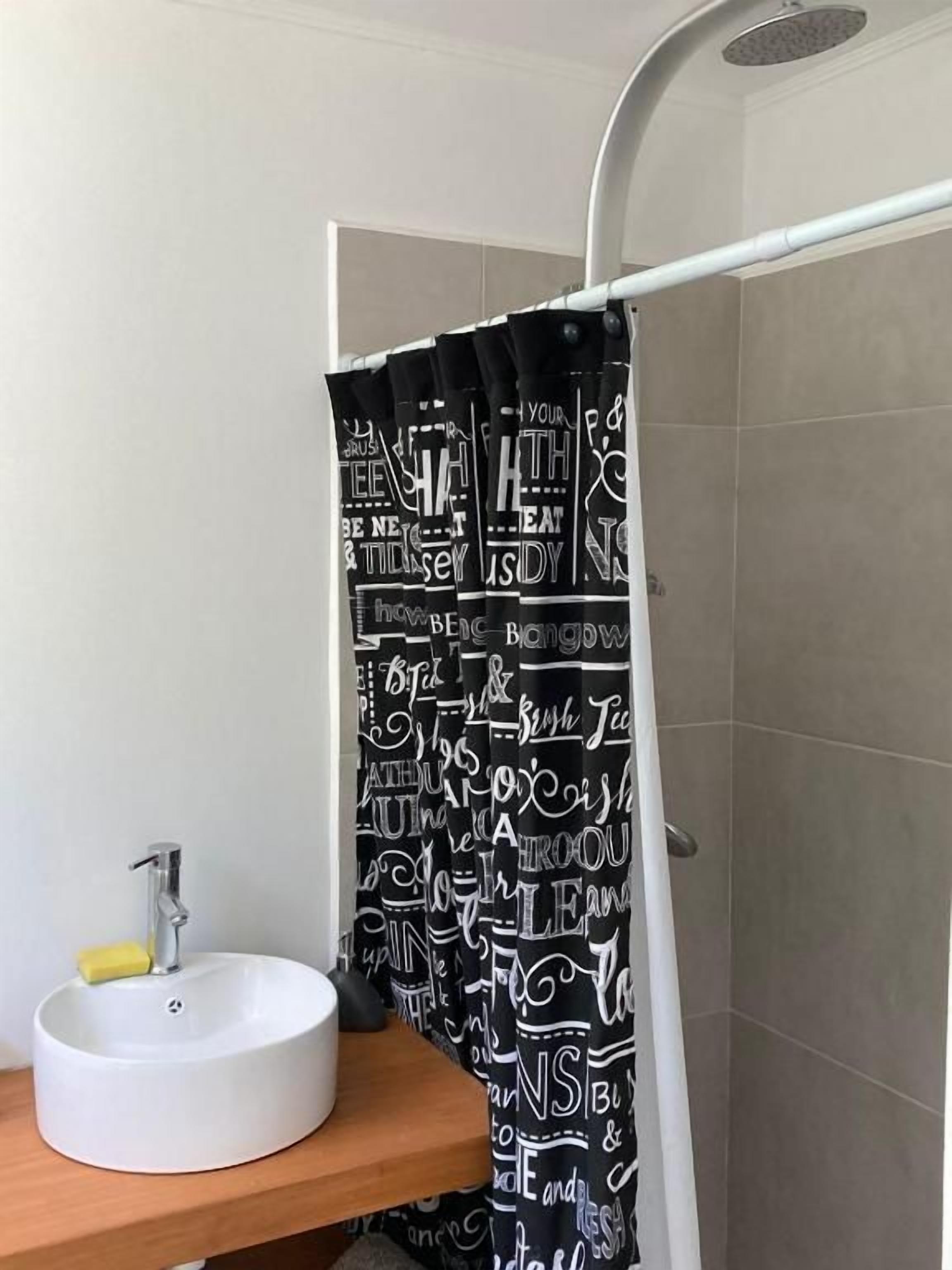 Casa de banho com uma pia branca, cortina de chuveiro com texto preto e chuveiro.