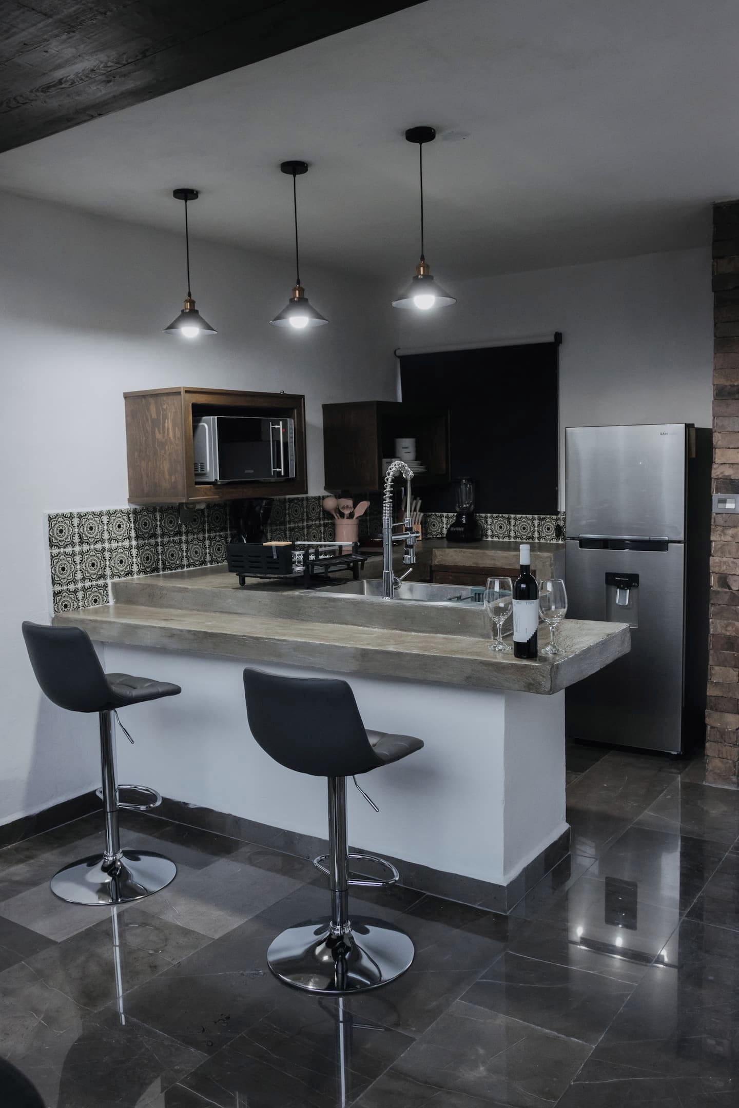 Cozinha moderna com ilha central, banquetas, iluminação pendente e eletrodomésticos de aço inoxidável.