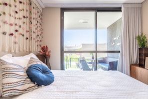 Quarto com cama grande, vista para o exterior por uma porta de correr e um painel de parede decorativo em macramé.