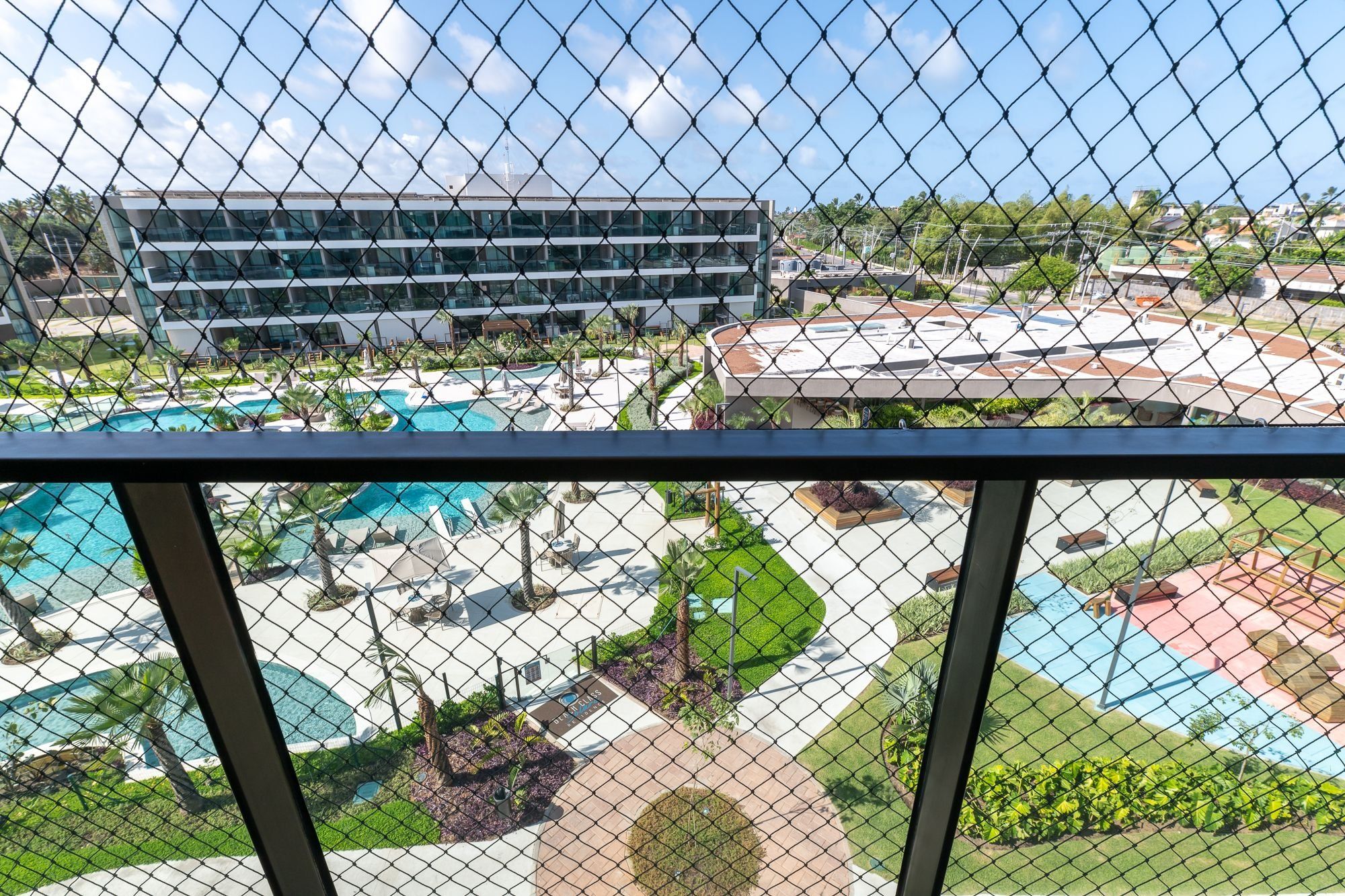 Vista de um hotel com piscina, um jardim bem cuidado e um edifício moderno ao fundo.