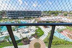 Vista de um hotel com piscina, um jardim bem cuidado e um edifício moderno ao fundo.